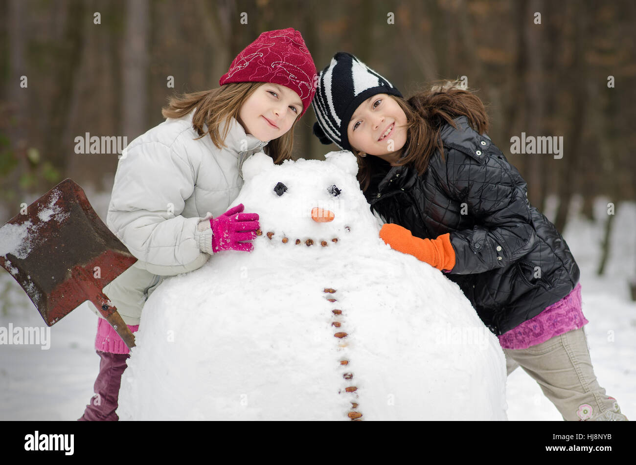 Two girls building a snowman Stock Photo - Alamy