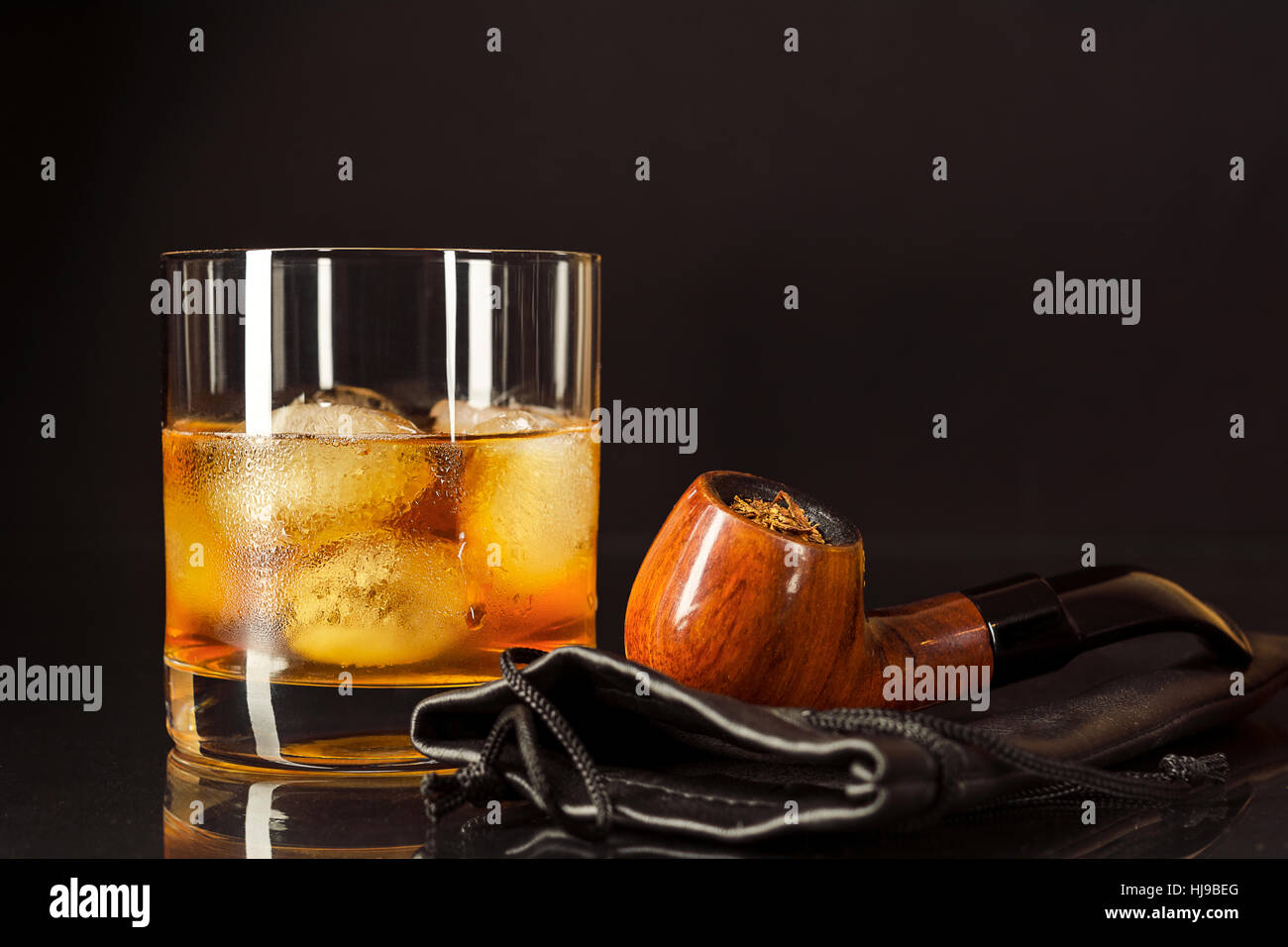 Scotch drink glass and smoking pipe on black background. Whiskey or ...