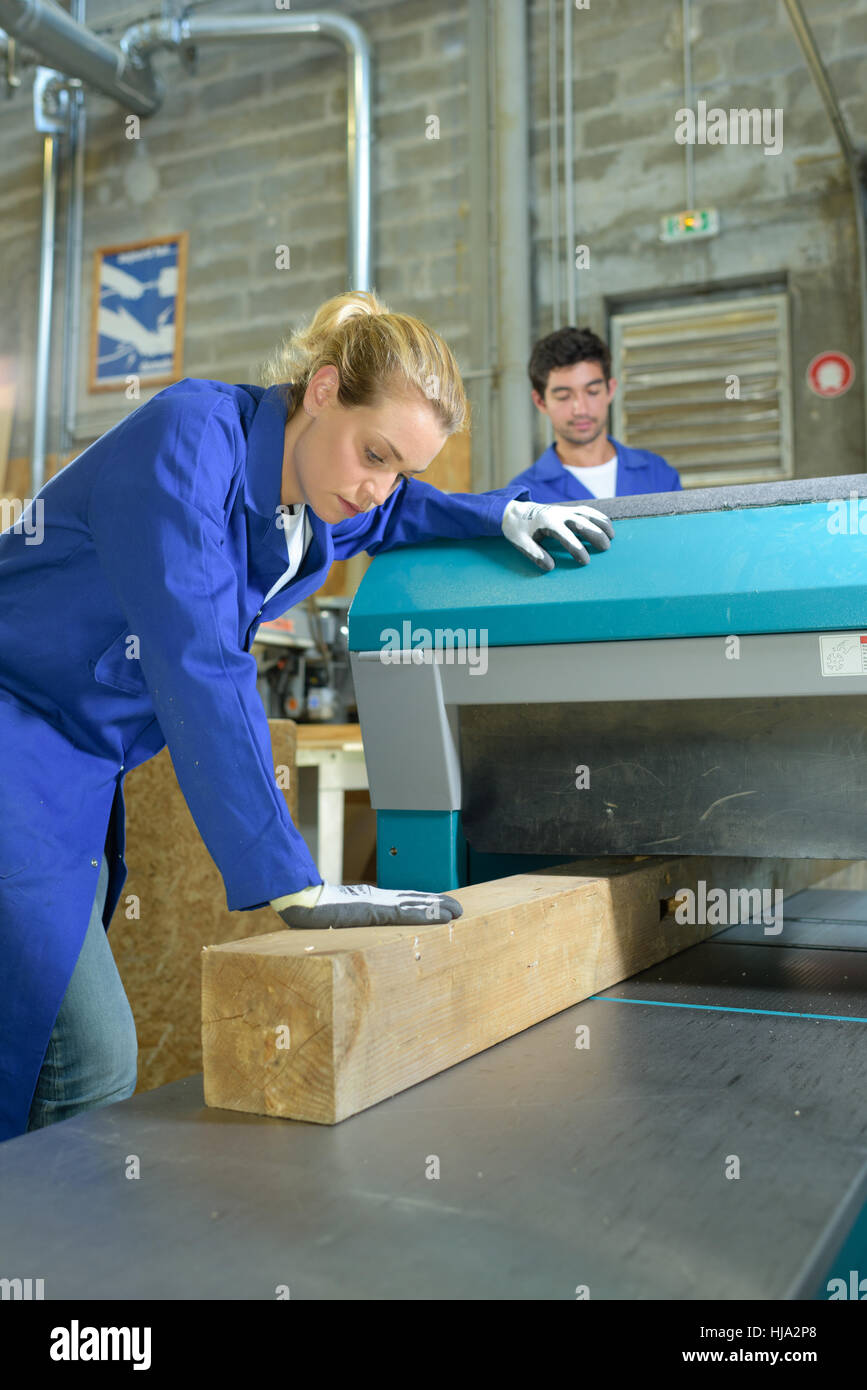 Worker guiding wooden beam through machine Stock Photo - Alamy