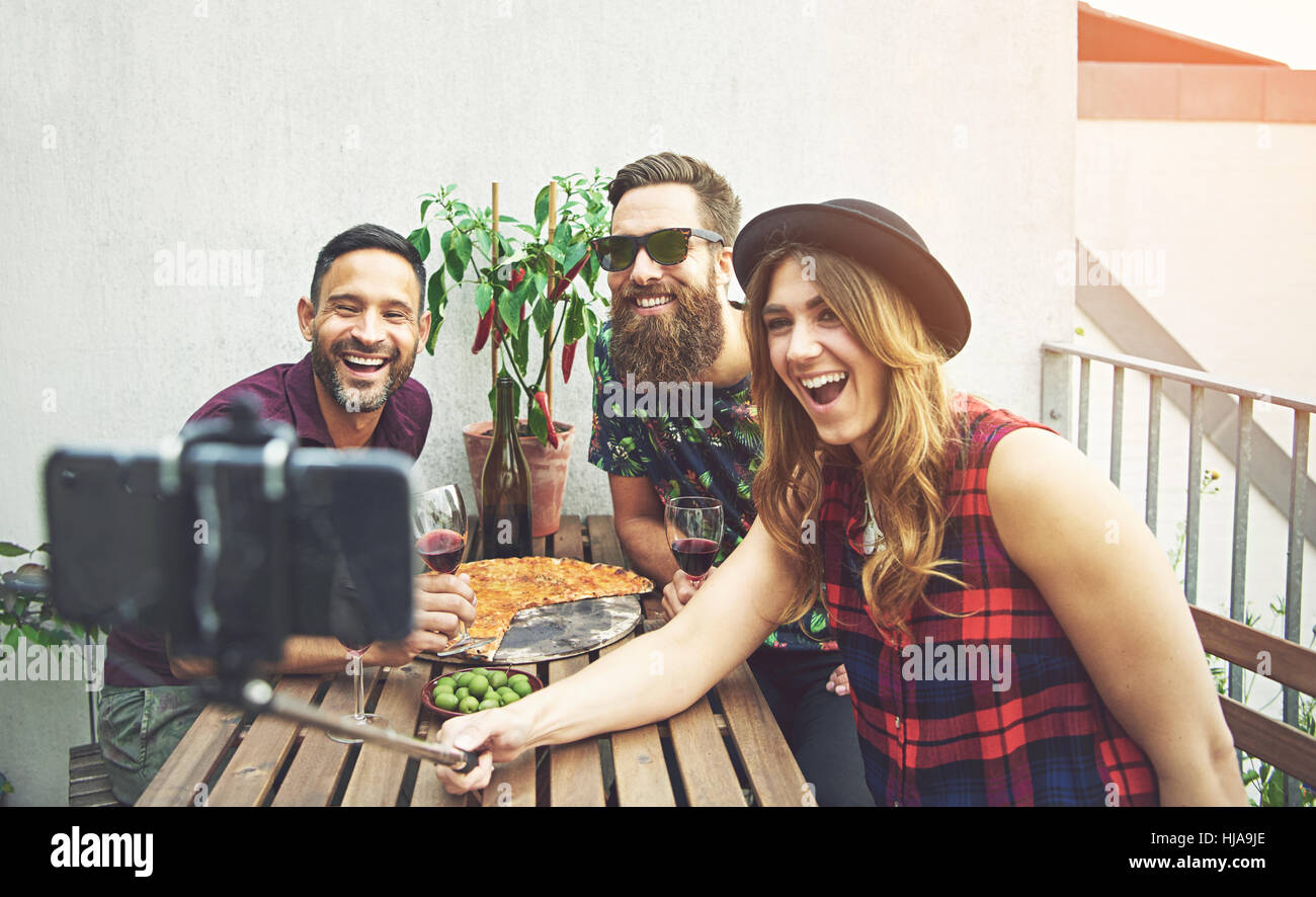 Friends use device to take self portrait photo while eating pizza and ...