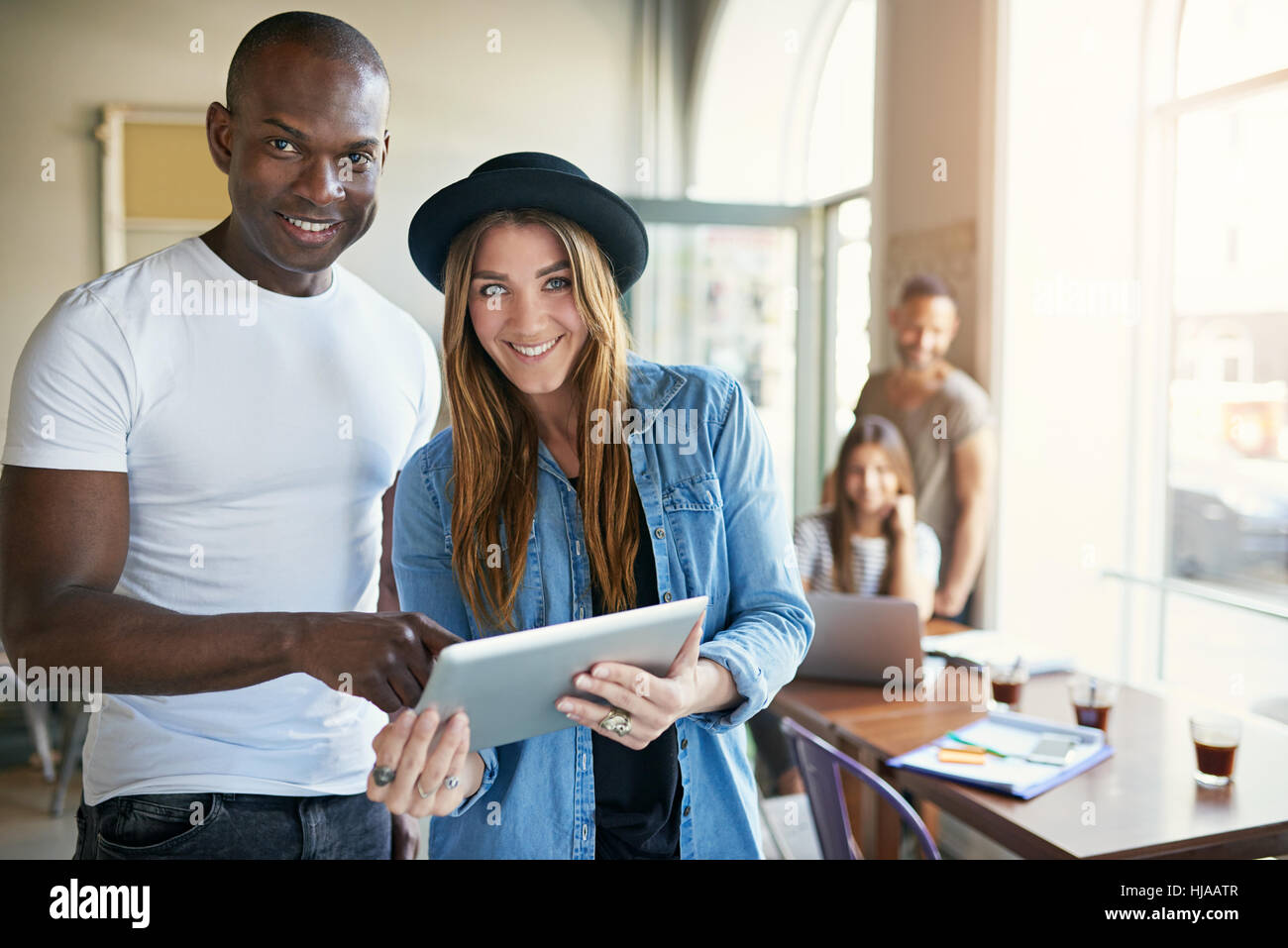 Two smiling multiracial co-workers using touch pad and smiling at ...