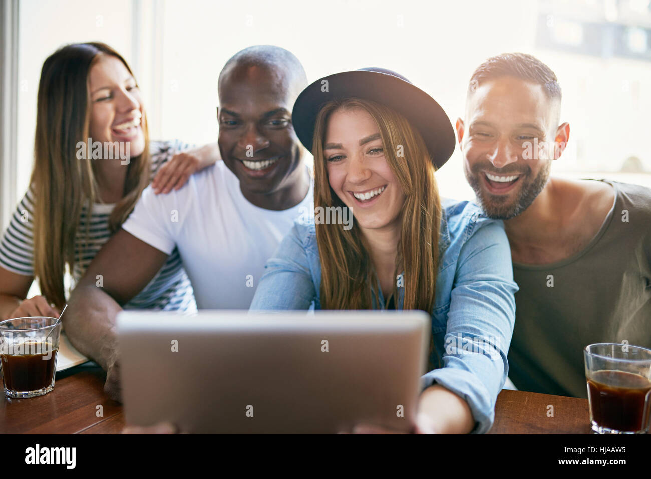 Four smiling young people sitting at table and having fun while sharing ...