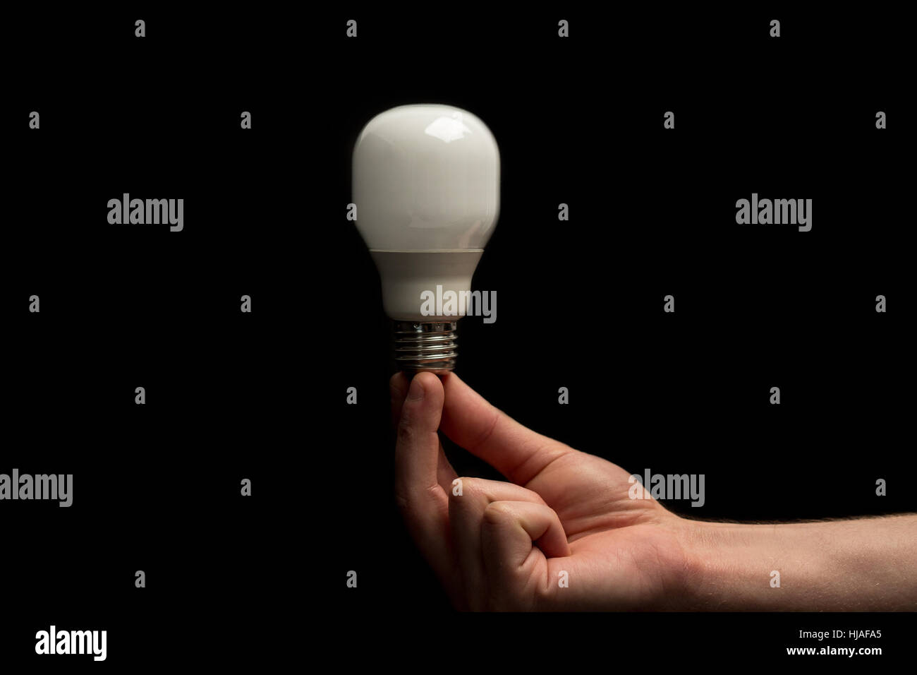 Man holding economic light bulb in his fingertips on black background ...