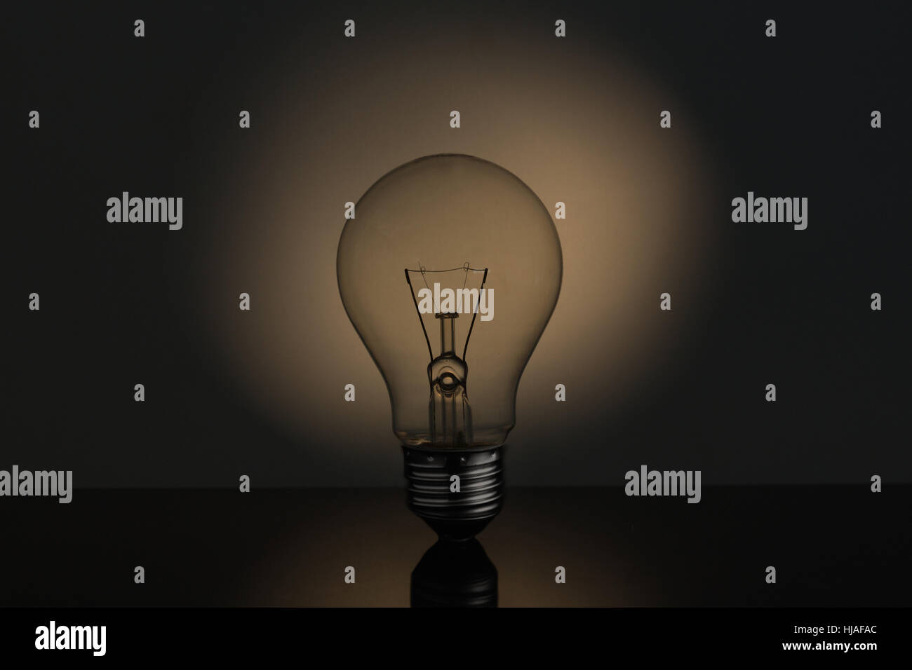 Big light bulb standing in sepia tones on reflective black surface ...