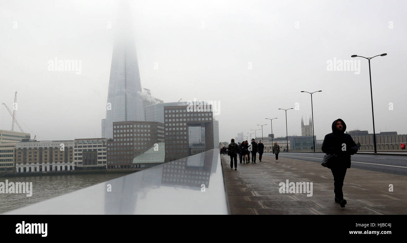 Pedestrians cross London Bridge with the Shard shrouded in fog behind ...