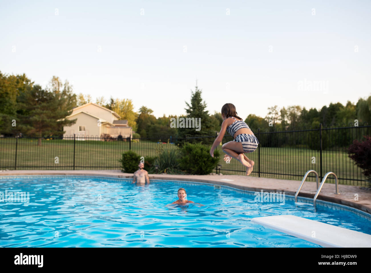Young girl jumping into swimming pool, father and grandmother watching ...