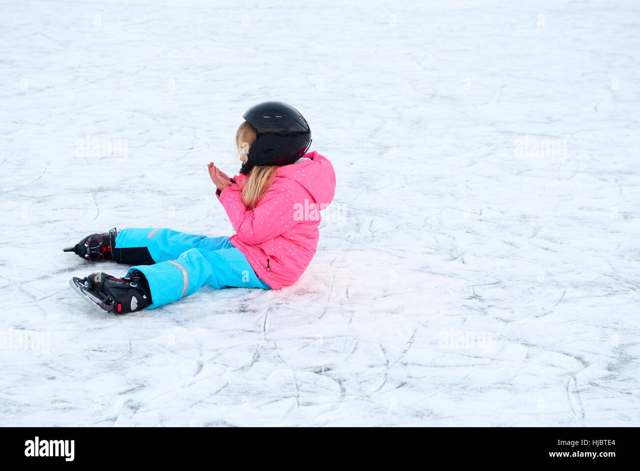 Child girl sitting on ice after falling in snowy park during winter ...
