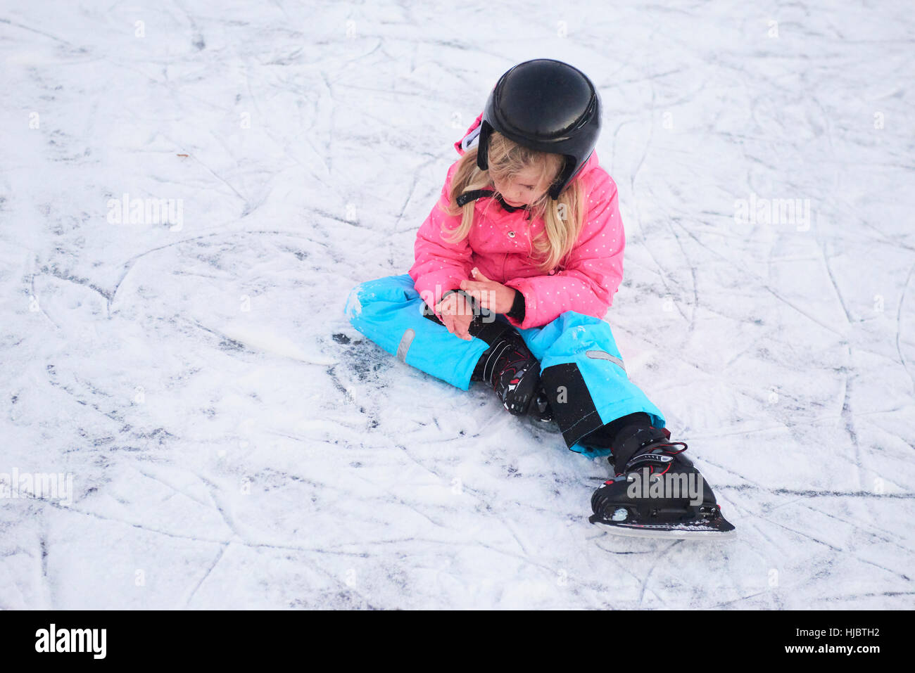 Child girl sitting on ice after falling in snowy park during winter ...