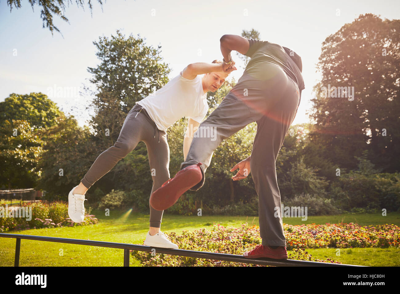 Man holding hands with personal trainer balancing on one leg on park ...