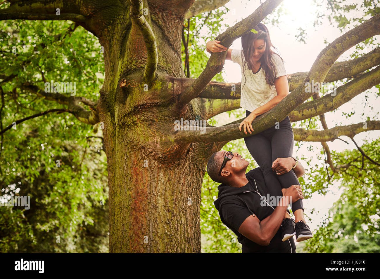 Personal trainer lifting woman to climb park tree Stock Photo - Alamy