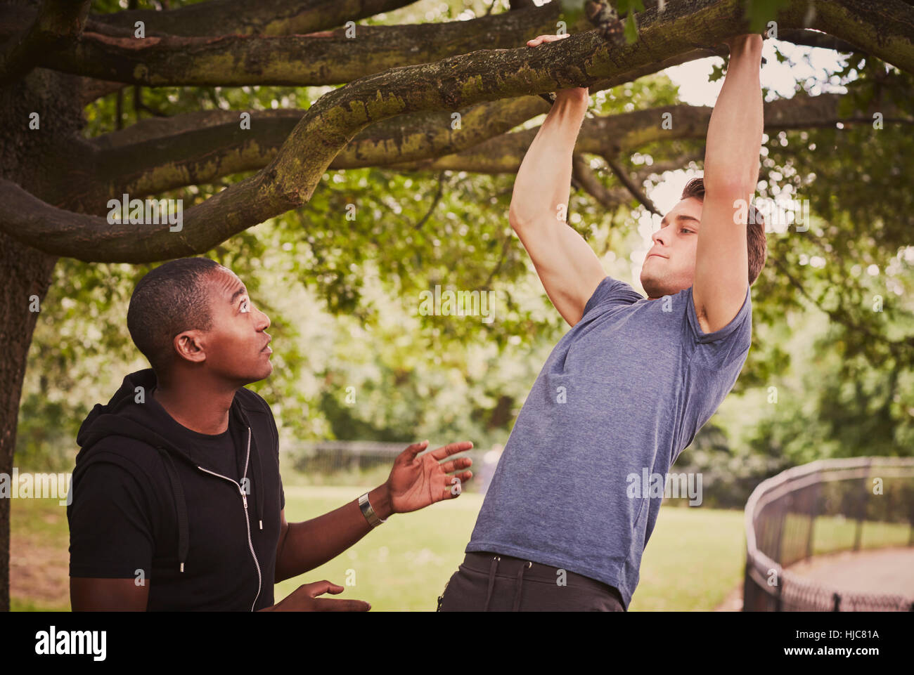 Personal trainer instructing man on pull ups using park tree branch ...