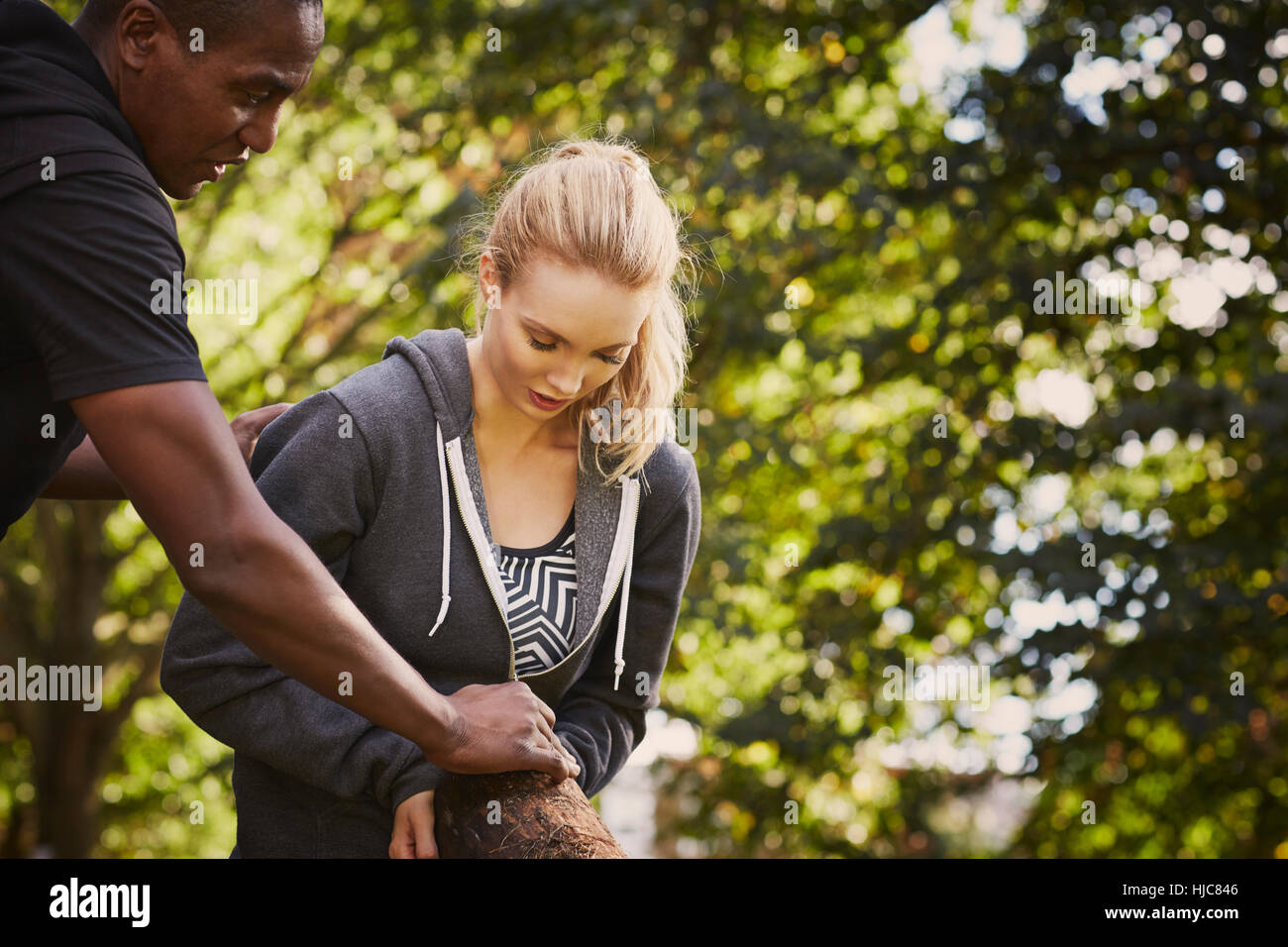 Young woman with personal trainer explaining tree trunk lift in park ...