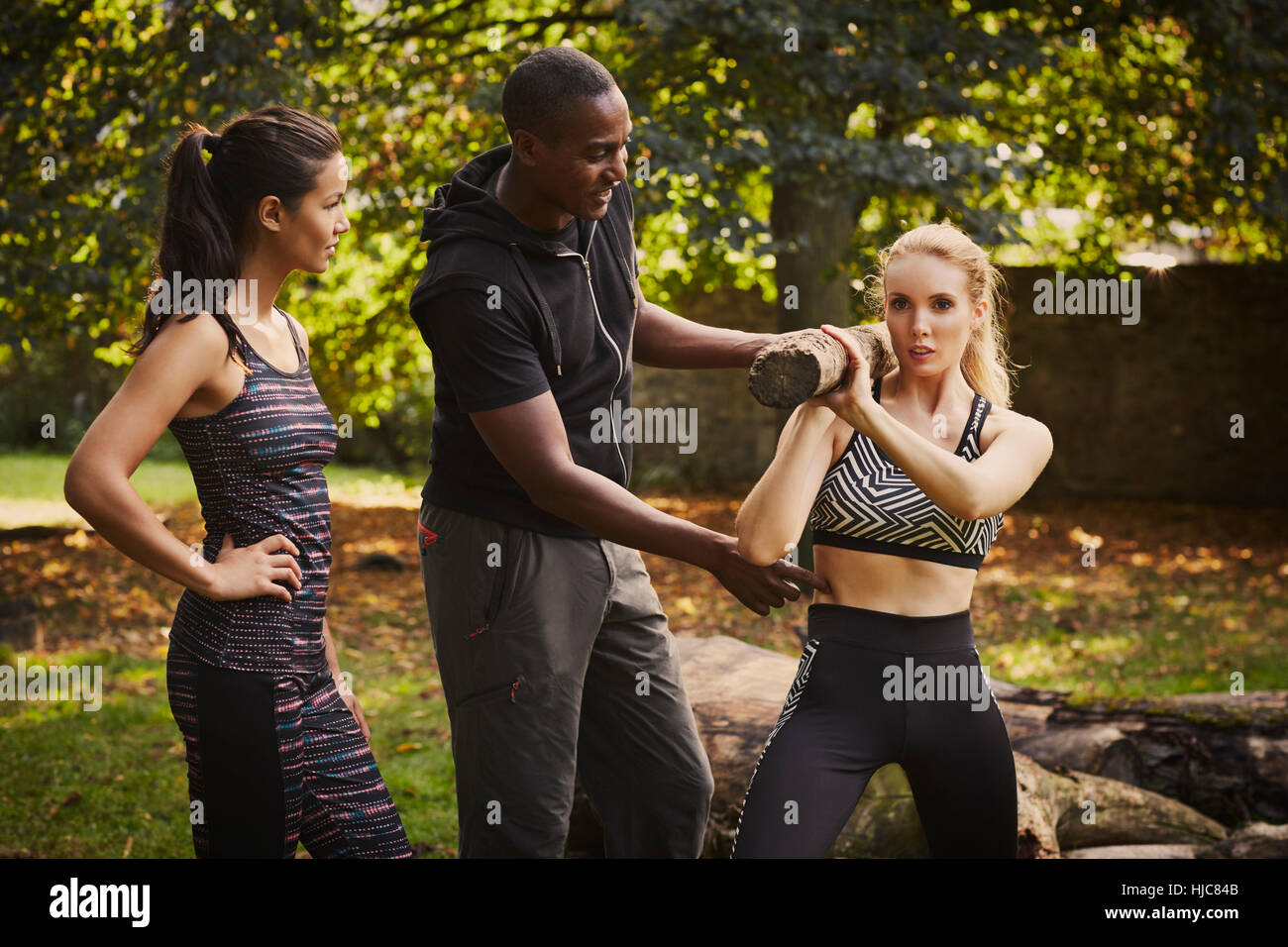 Two women with personal trainer explaining tree trunk shoulder lift in ...