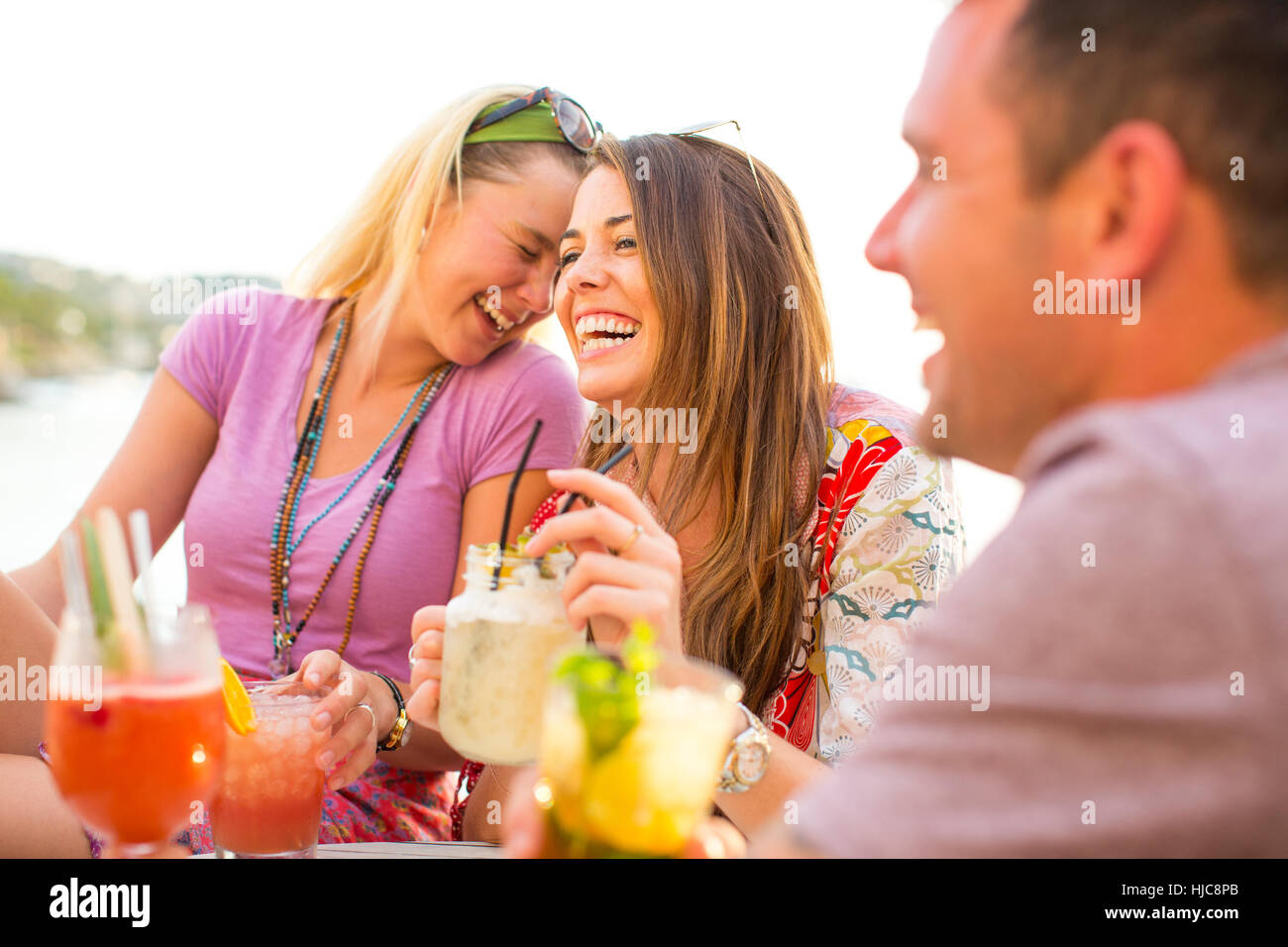 Three adult friends laughing over cocktails at waterfront restaurant ...