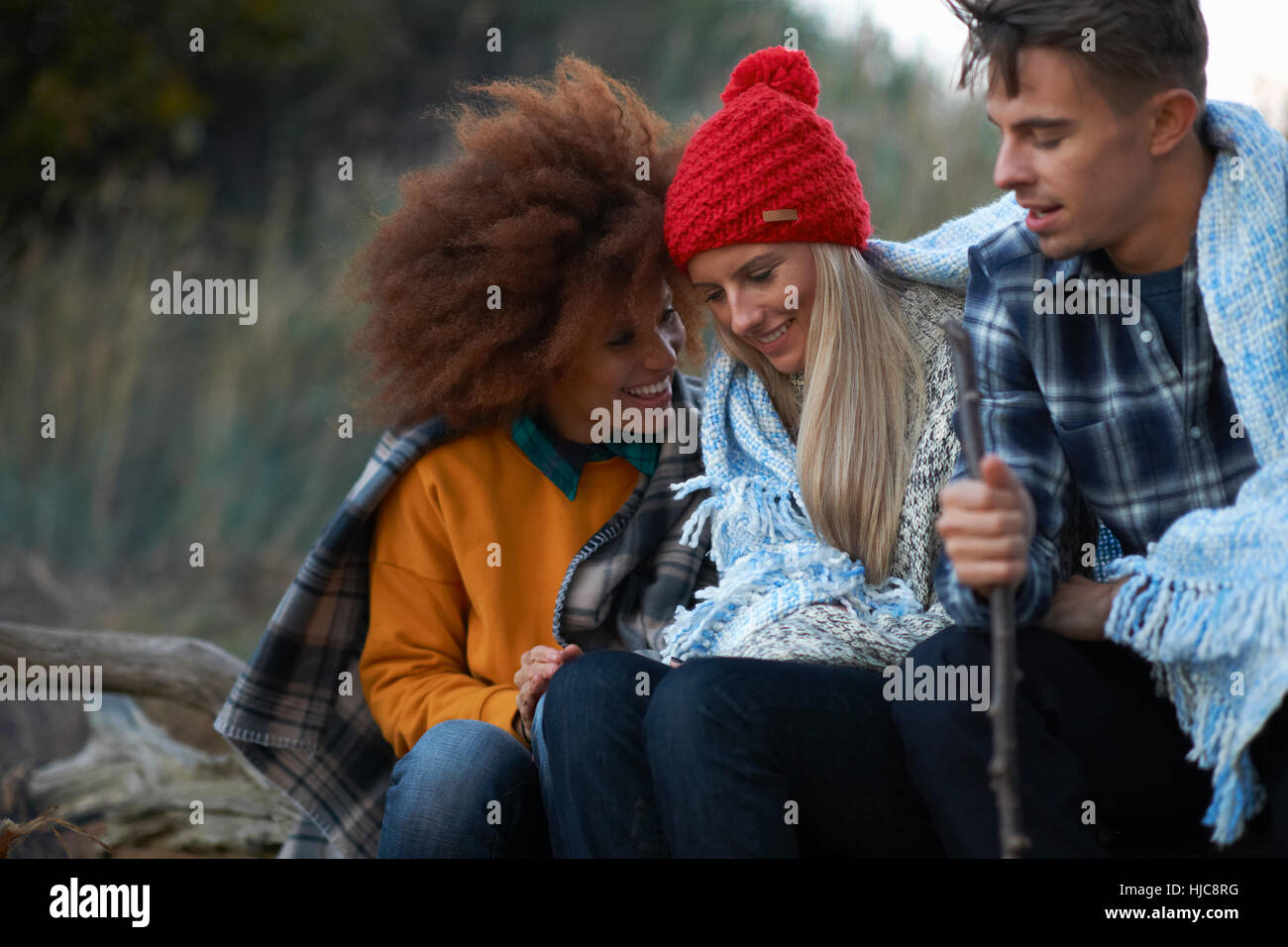 Three adult friends sitting huddled together on beach at dusk Stock ...