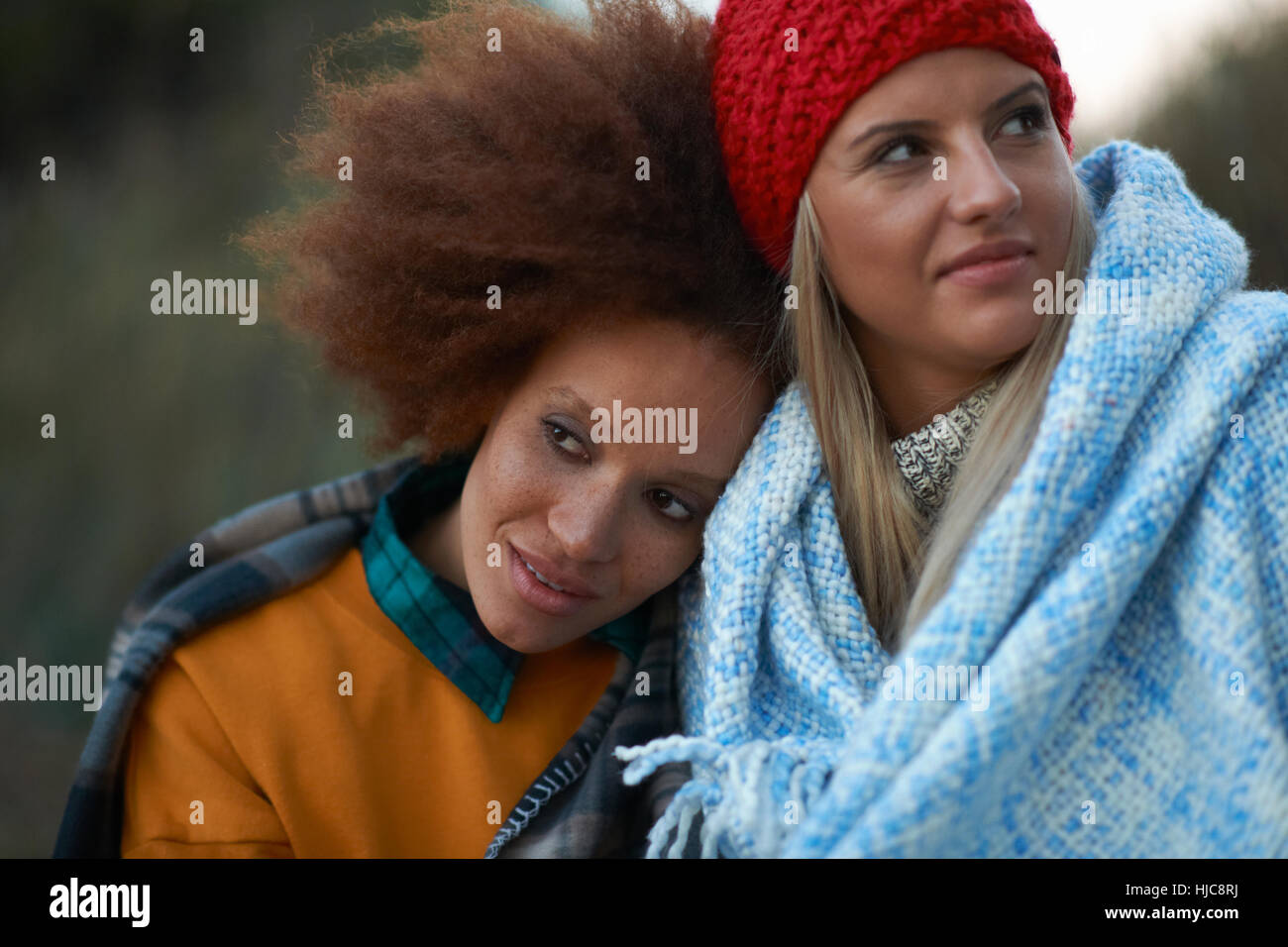 Portrait of two young women huddled in blanket on beach at dusk Stock ...