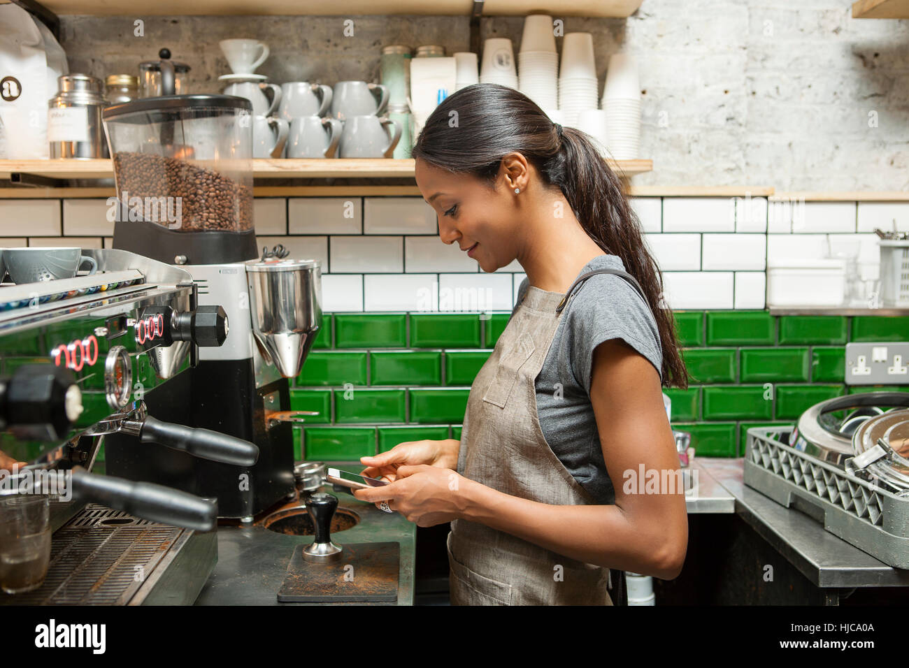 Female barista looking at smartphone in cafe kitchen Stock Photo - Alamy