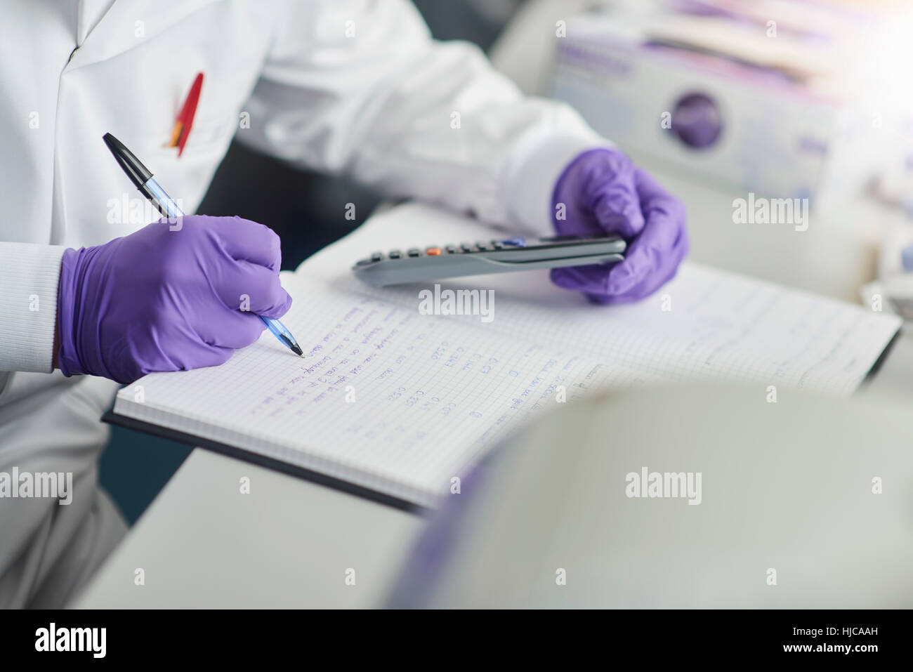 Scientist using calculator writing in notebook Stock Photo - Alamy