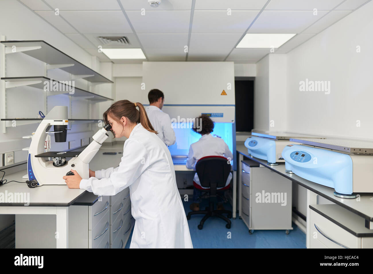 Woman in lab coat looking through microscope hi-res stock photography ...