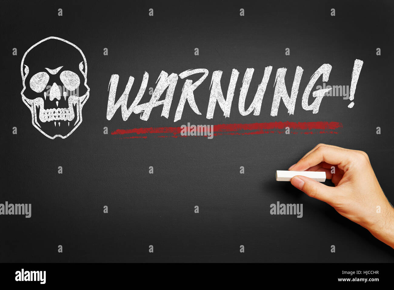 Hand with chalk writing in German "Warnung!" (warning) on a blackboard ...