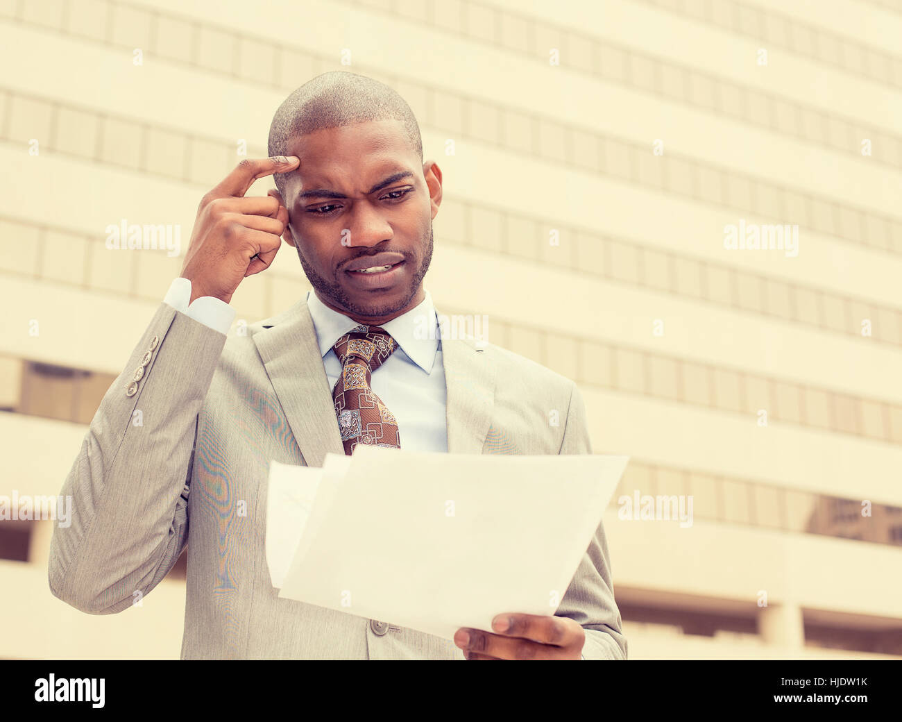 Confused executive man looking at documents outside corporate office ...