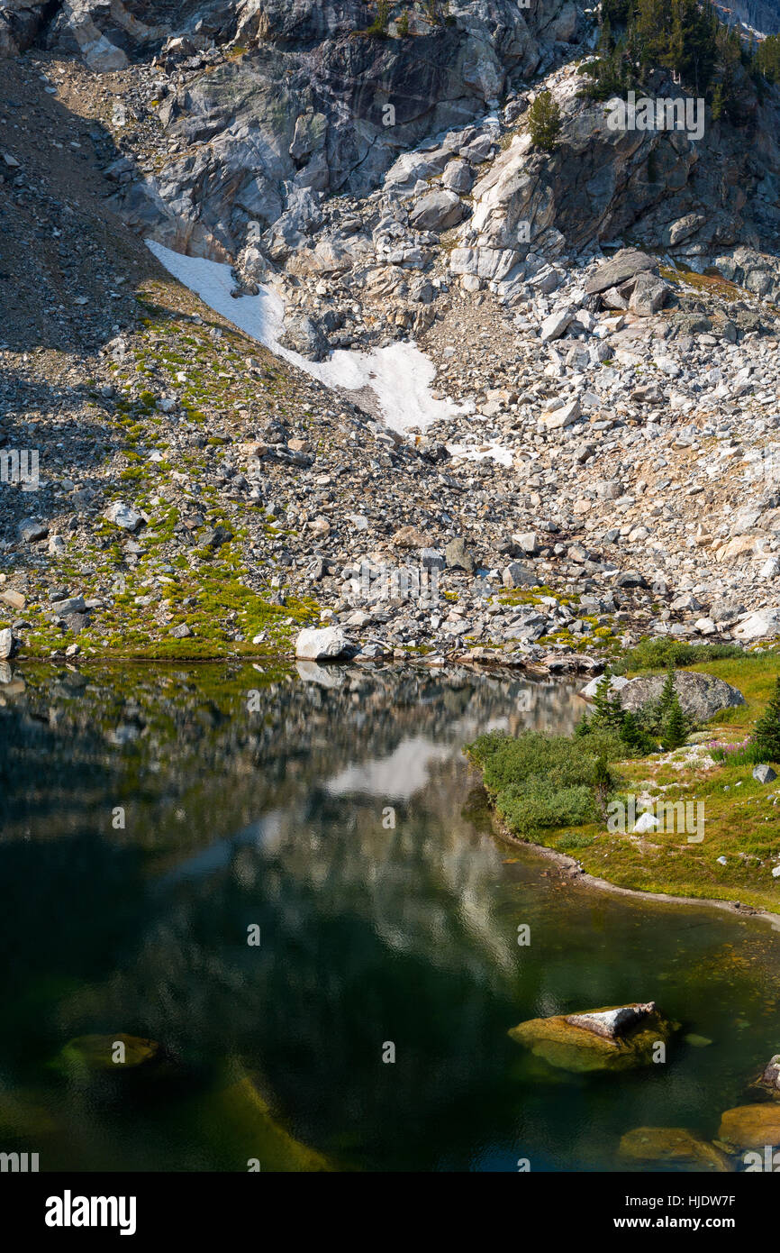 An alpine scree field pouring boulders into Ramshead Lake in the Teton ...