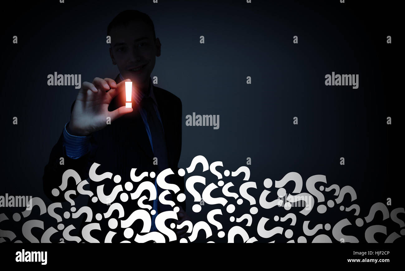 Young businessman on dark background taking exclamation mark with ...