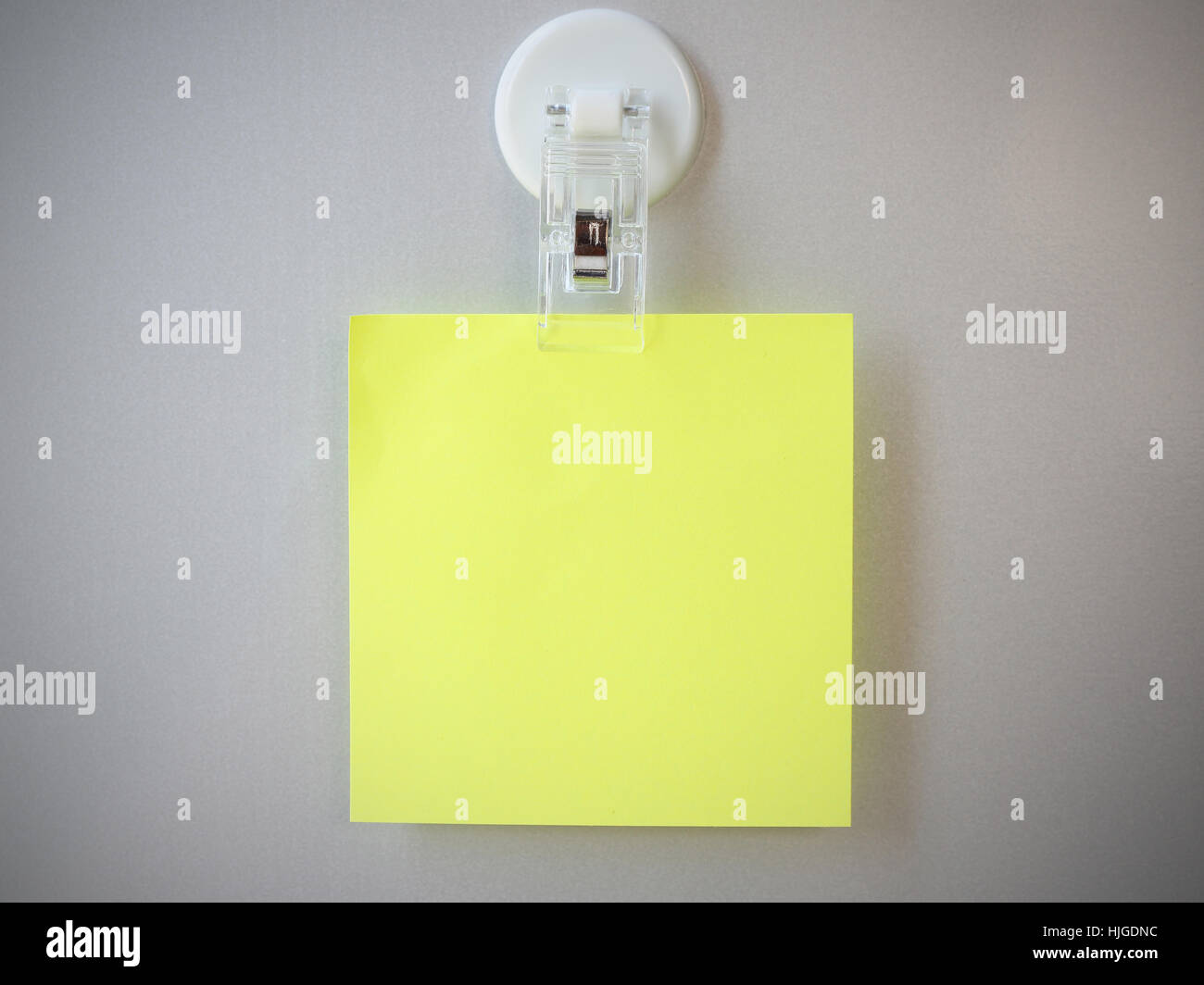 Yellow post it clip by clip magnet on gray refrigerator background ...