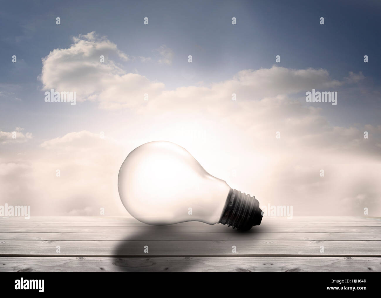 Light bulb resting on floorboards in the blue cloudy sky with sunlight ...