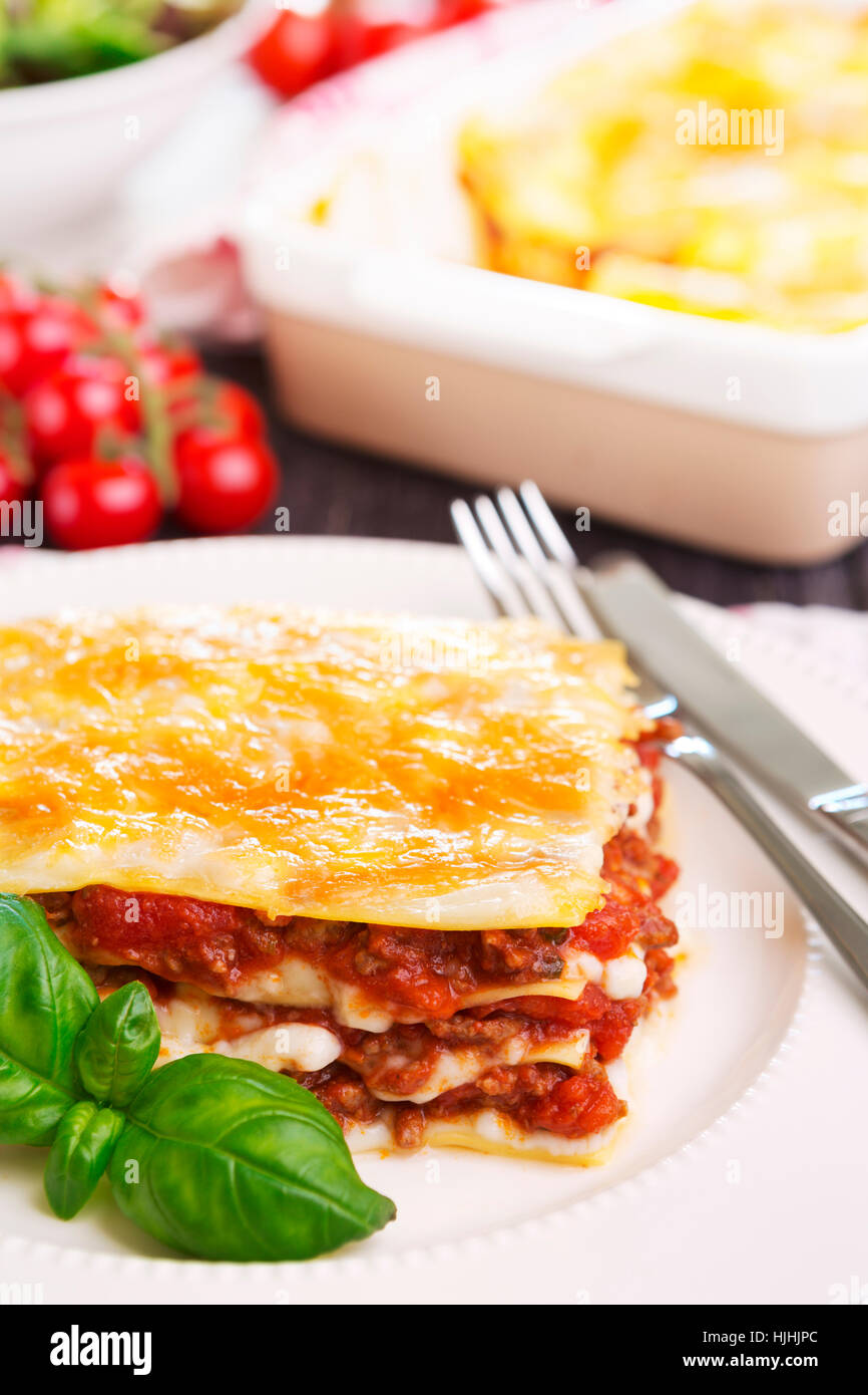A portion of homemade lasagna on a plate on a brightly lit table Stock ...