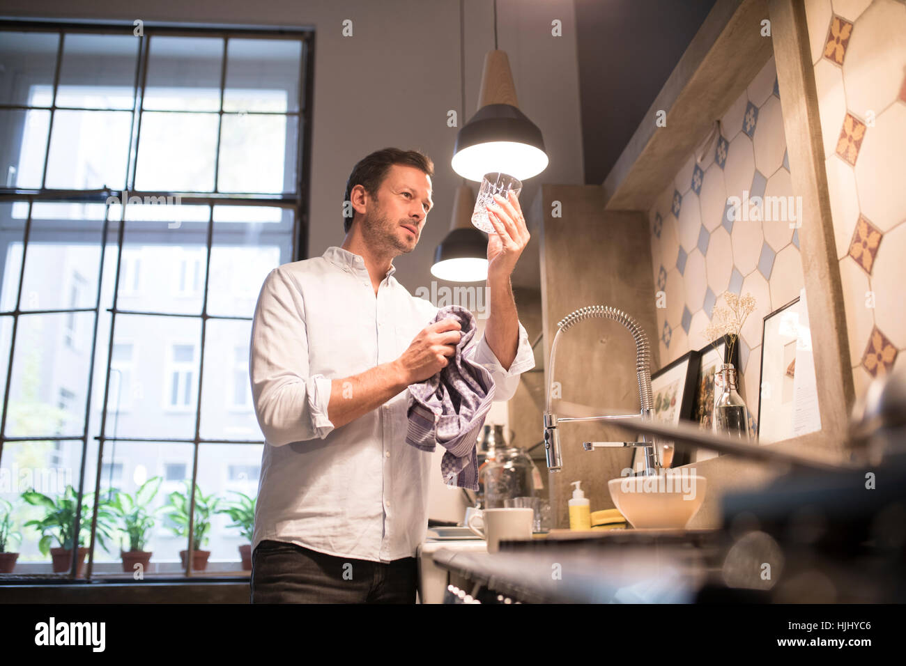 Man in kitchen drying glass with towel Stock Photo - Alamy