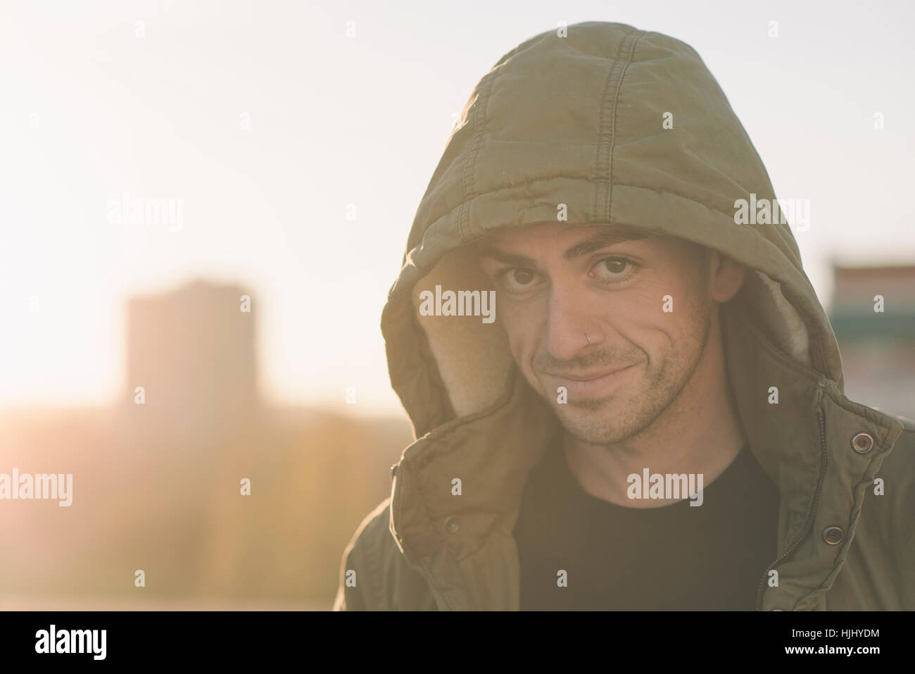 Portrait of smiling man wearing hooded jacket outdoors at sunset Stock ...