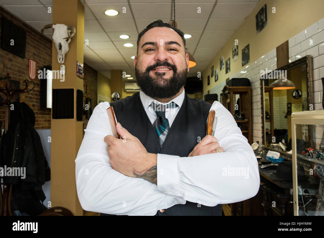 Barber with arms crossed holding a straight razor and comb in a ...