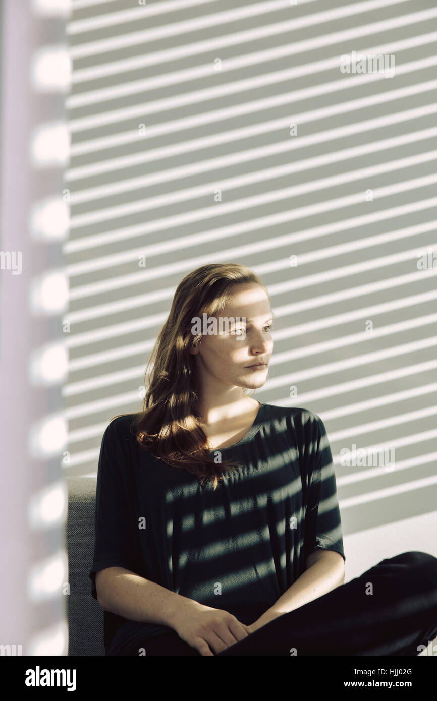 Portrait of serious young woman sitting in a shadowed room Stock Photo ...