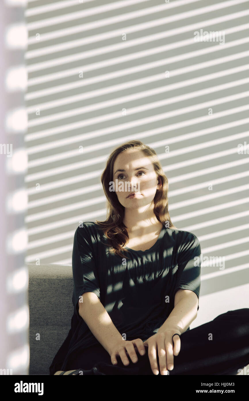 Portrait of young woman sitting in a shadowed room Stock Photo - Alamy