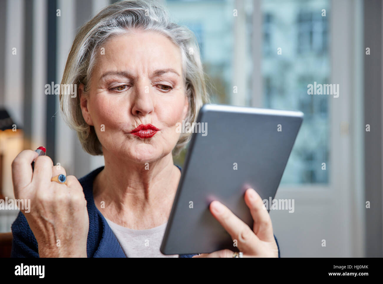 Senior woman applying lipstick holding tablet Stock Photo - Alamy