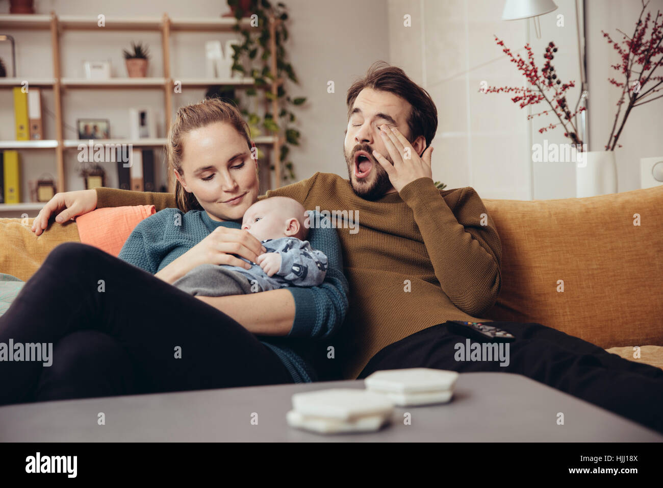 Tired father and mother sitting with baby on couch Stock Photo - Alamy