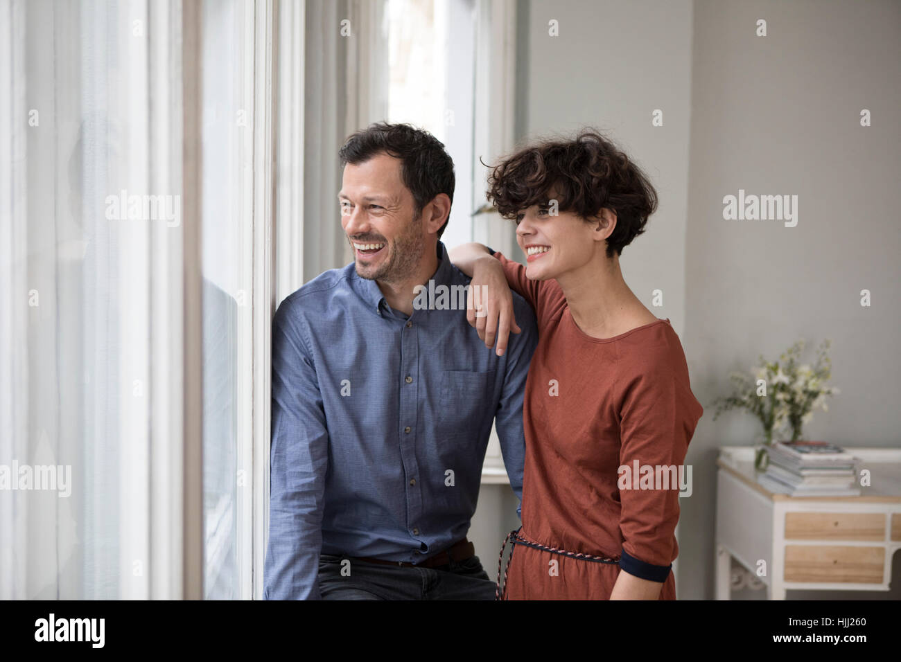 Laughing couple looking through window at home Stock Photo - Alamy