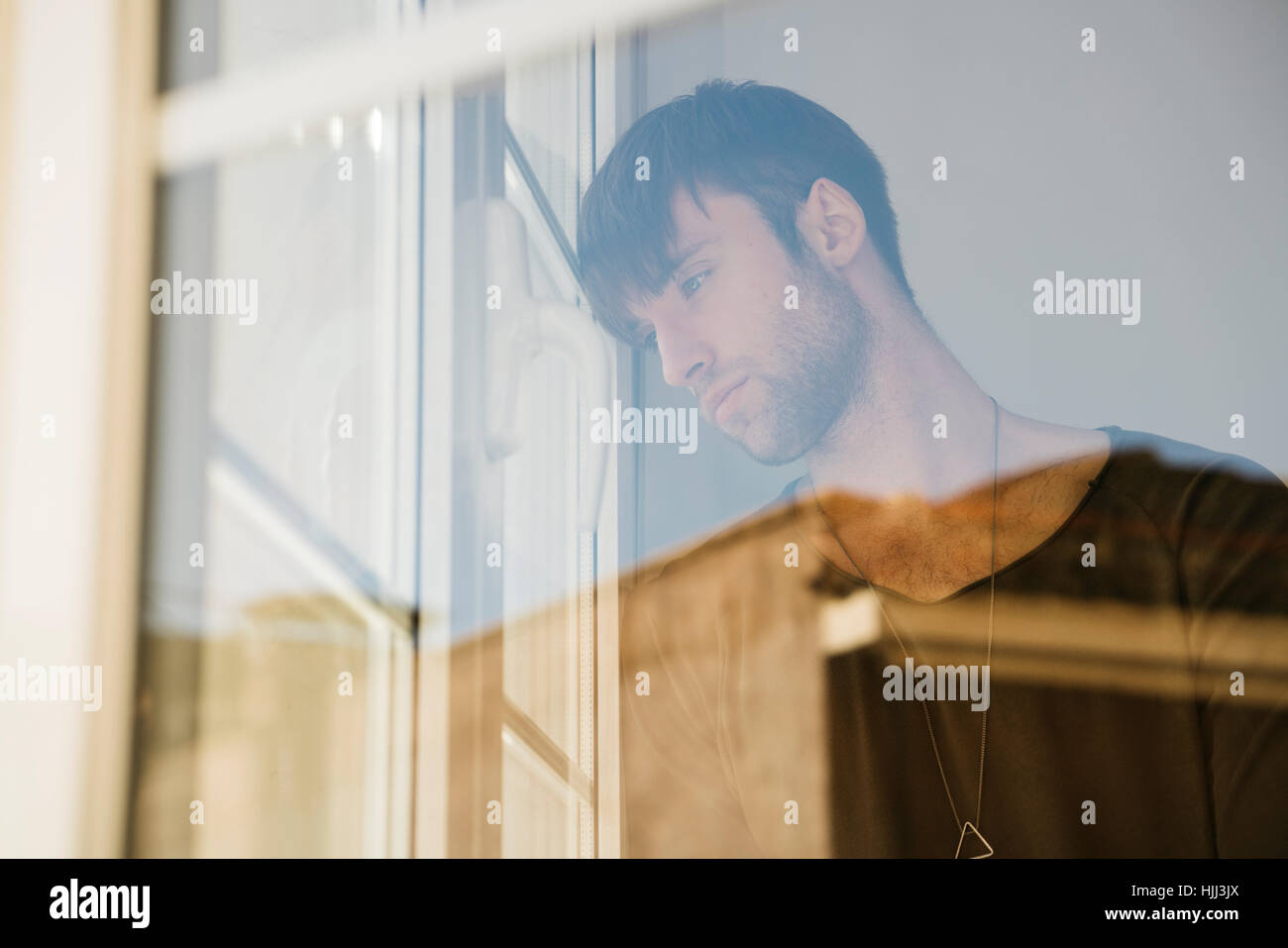Sad young man looking through window Stock Photo - Alamy
