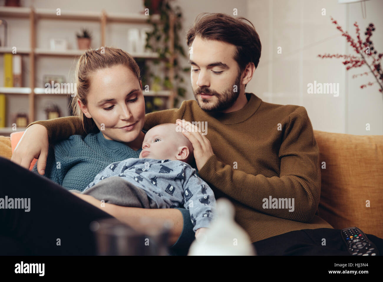 Father and mother cuddling with baby on couch Stock Photo - Alamy