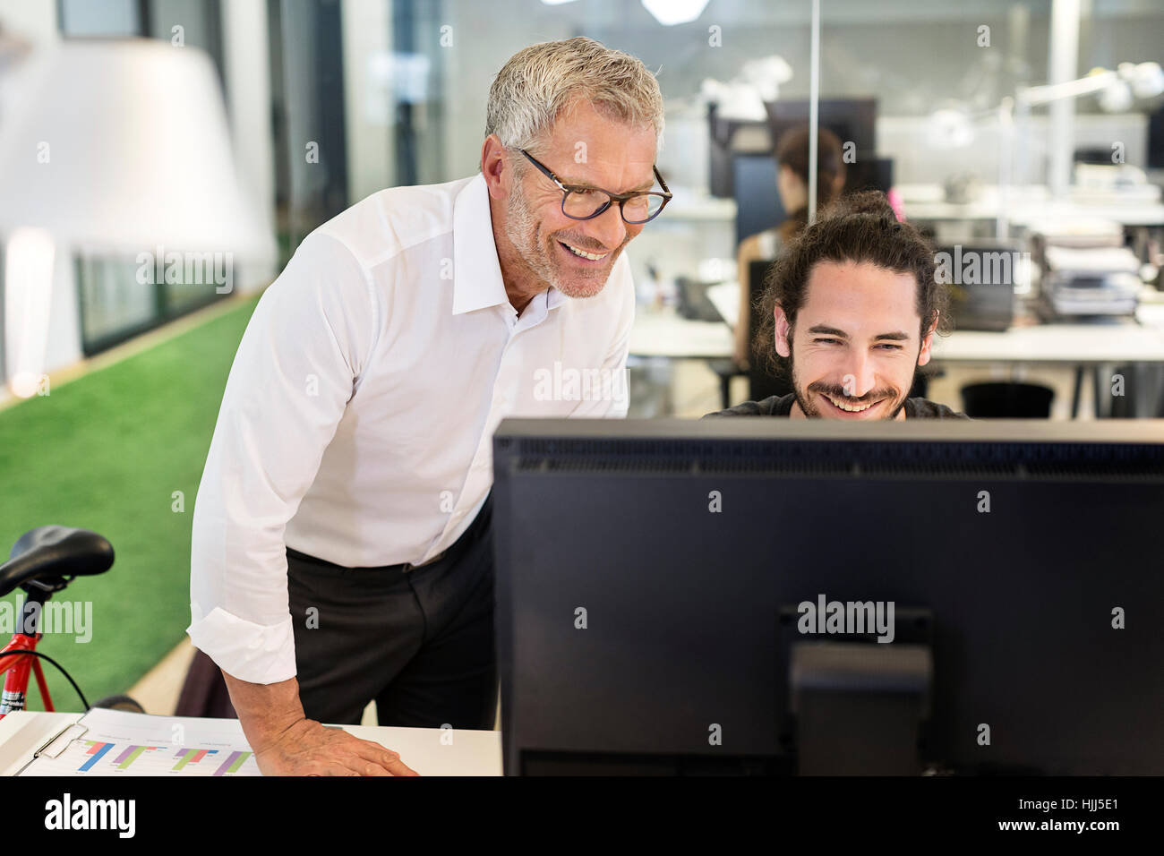 Two smiling men in office looking at computer monitor Stock Photo - Alamy