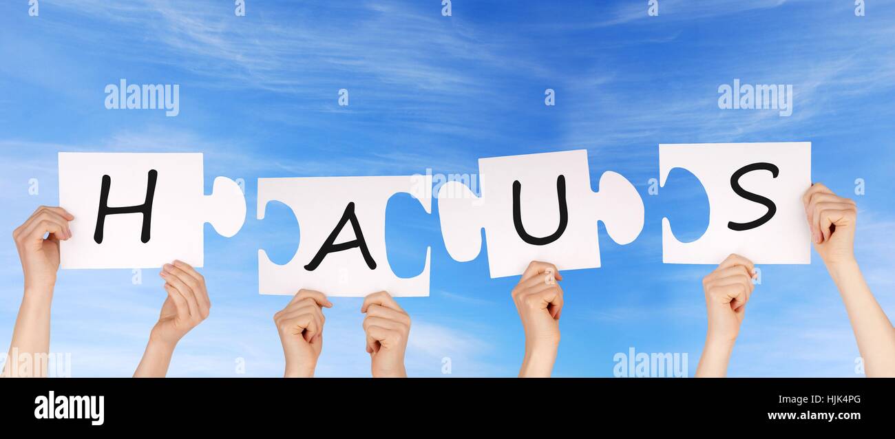 hands holding four pieces of a puzzle with the german word HAUS, which ...