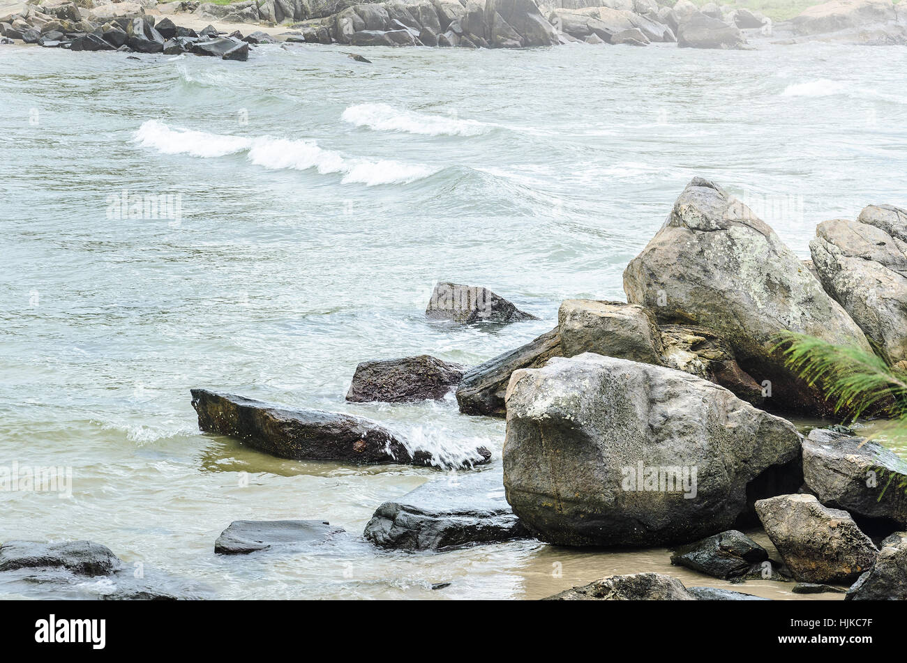 Several large rocks near the beach, some small waves in the sea water ...