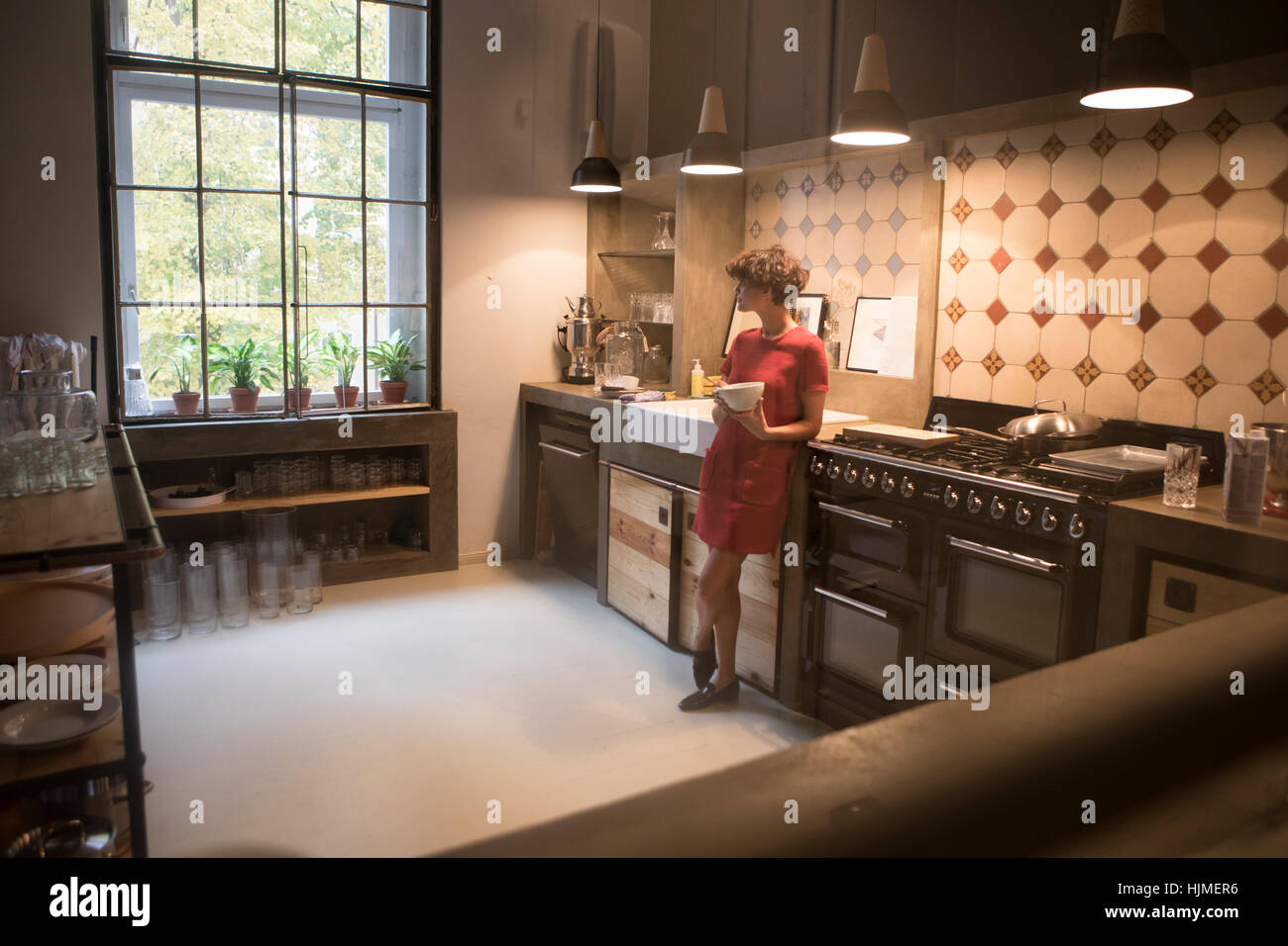 Young woman standing in the kitchen looking through window Stock Photo ...