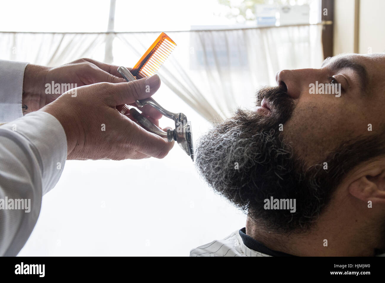Barber cutting man's beard Stock Photo - Alamy