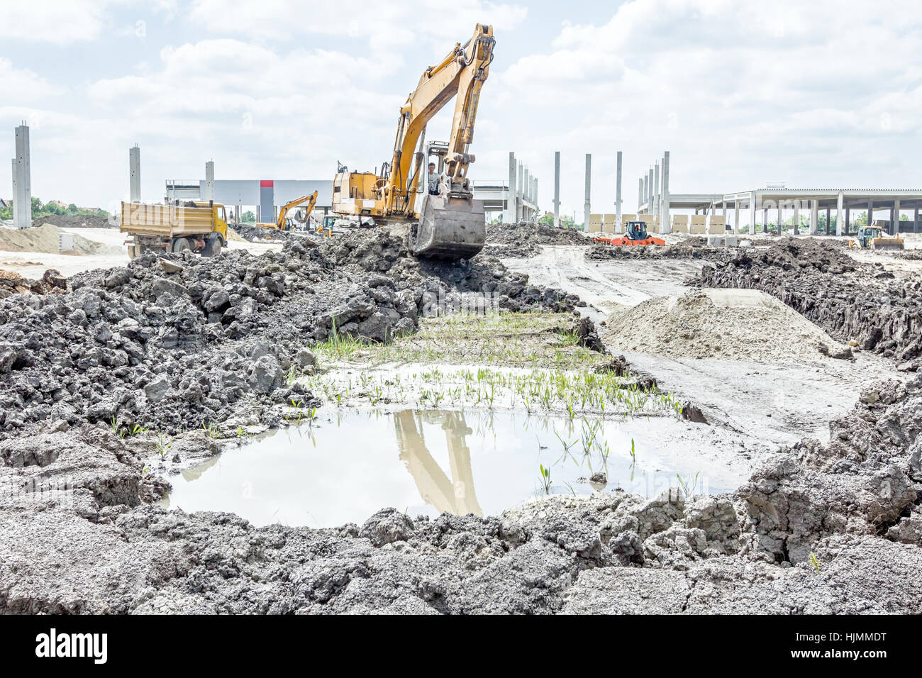 Yellow excavator is making pile of soil by pulling ground up on heap at ...