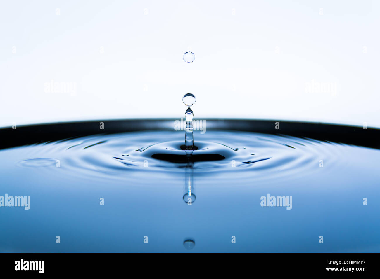 Drop of water falling into blue water surface with concentric waves and ...