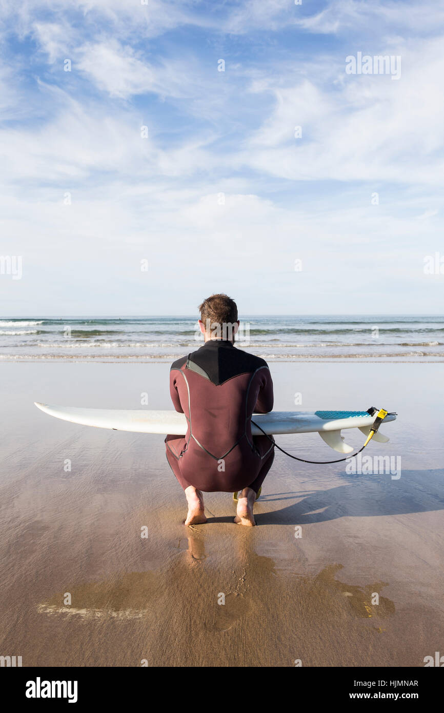 Man with surfboard crouching on the beach Stock Photo - Alamy