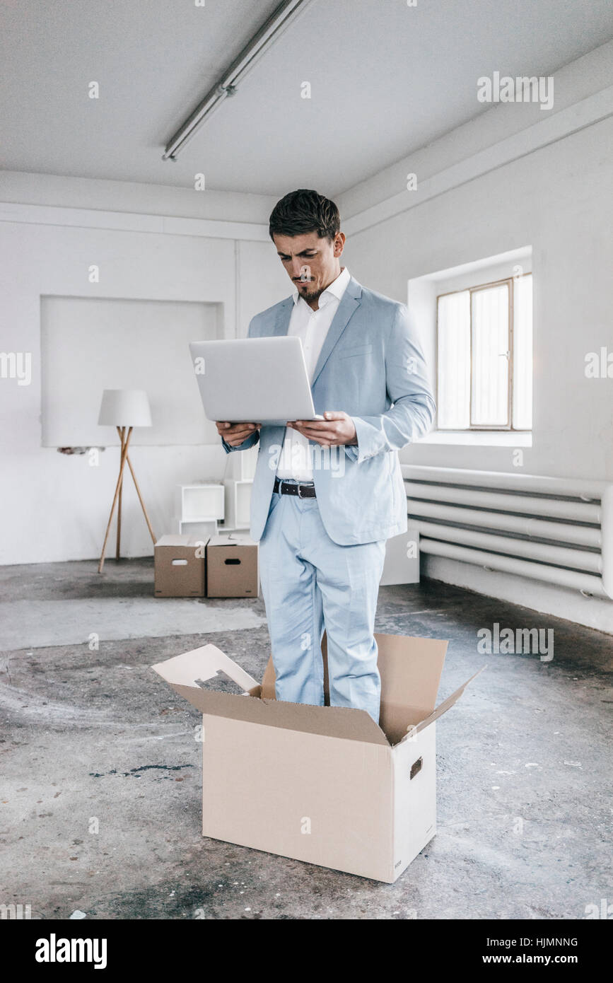 Businessman using laptop inside cardboard box in empty loft Stock Photo ...