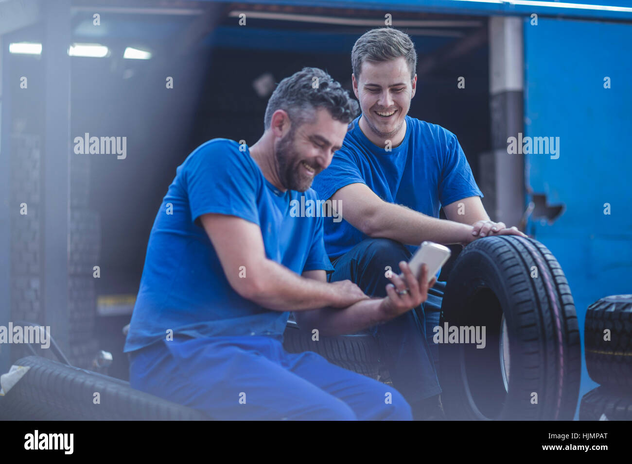 Two mechanics on a break looking at cell phone Stock Photo - Alamy